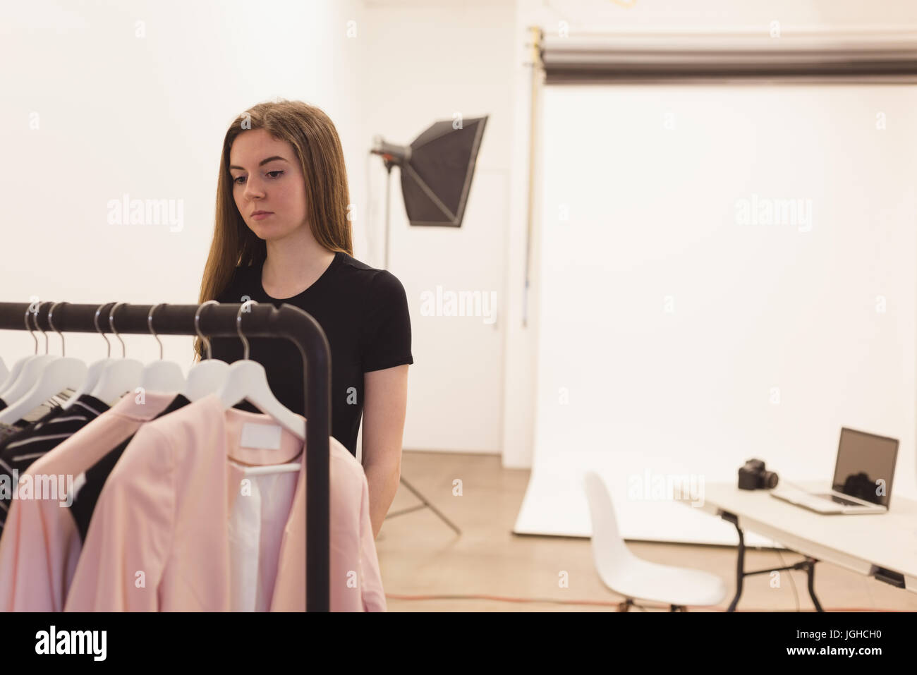 Female model choosing clothes hanging on rack at studio Stock Photo - Alamy
