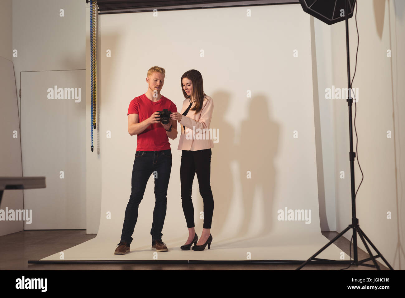 Full length of photographer with model holding camera against backdrop ...