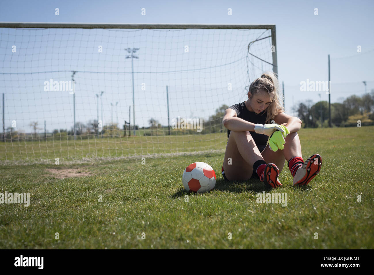 Full length of tired female soccer player relaxing on playing field ...
