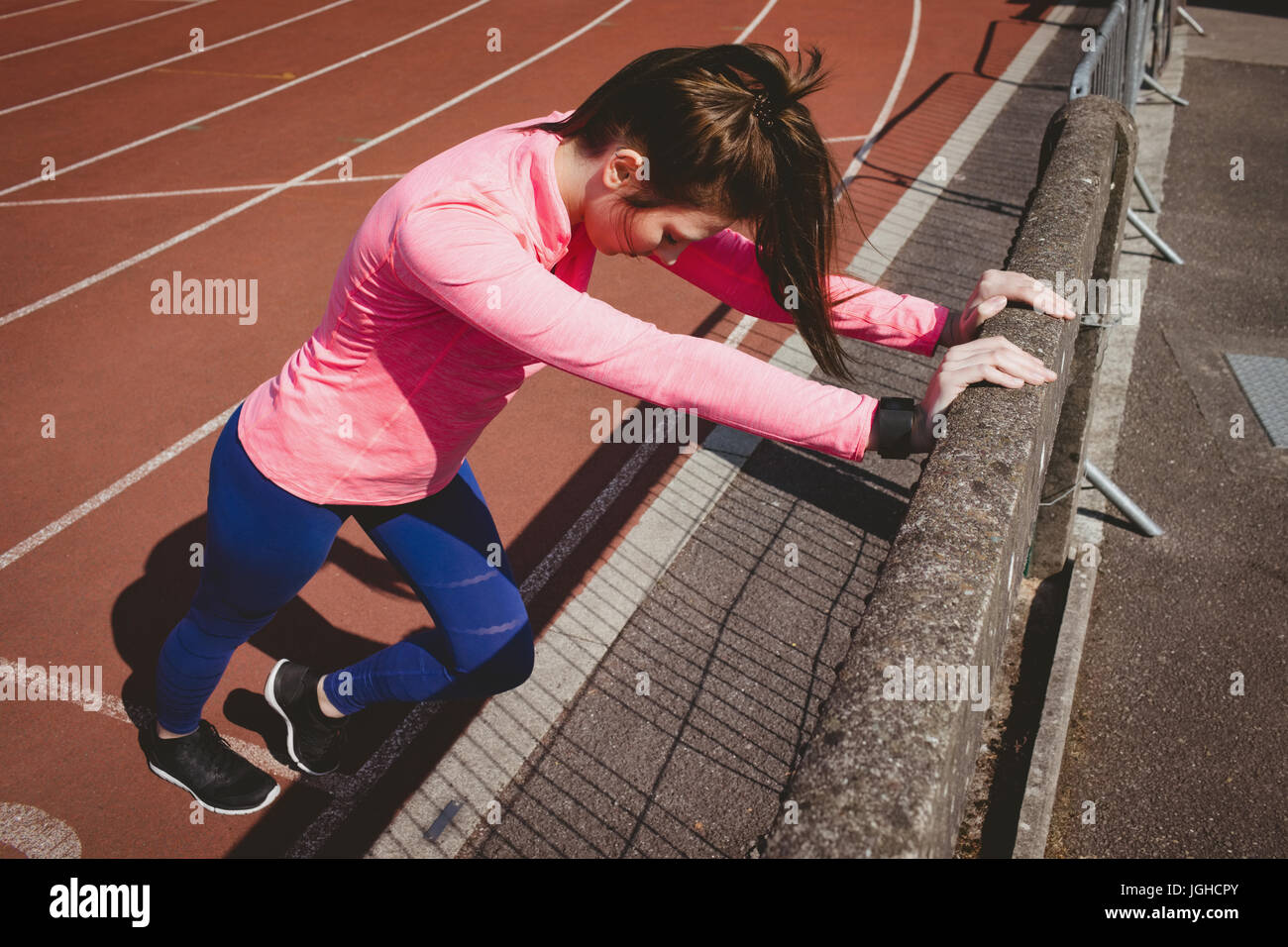 Full length of female athlete exercising by railing on running track ...