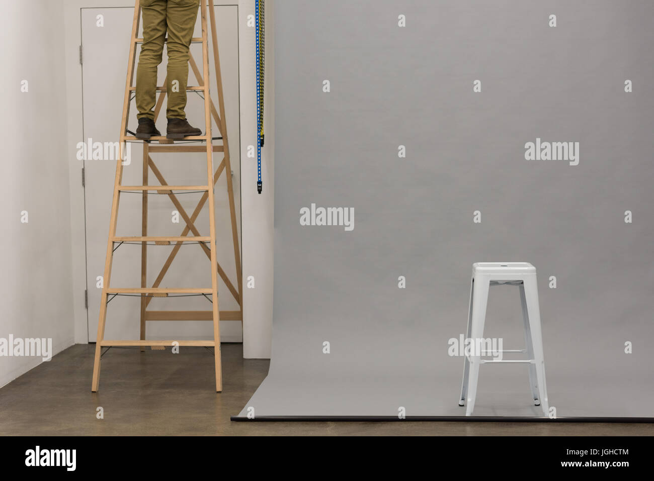 Low section of male photographer standing on step ladder by backdrop at ...