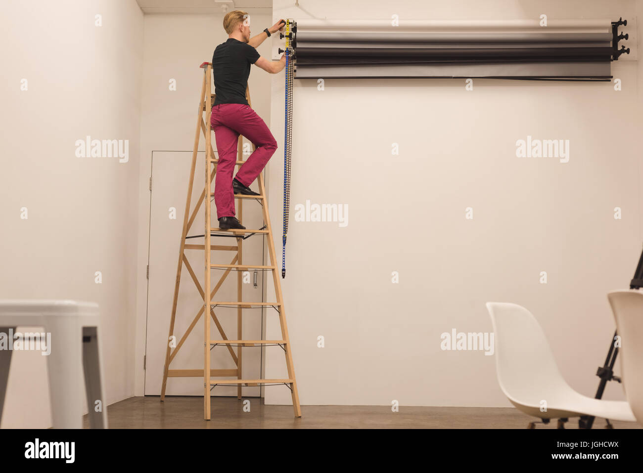 Full length of male photographer on ladder adjusting backdrop at studio ...