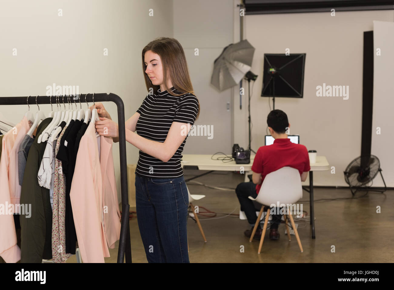 Young model choosing clothes on rack with photographer sitting on chair ...