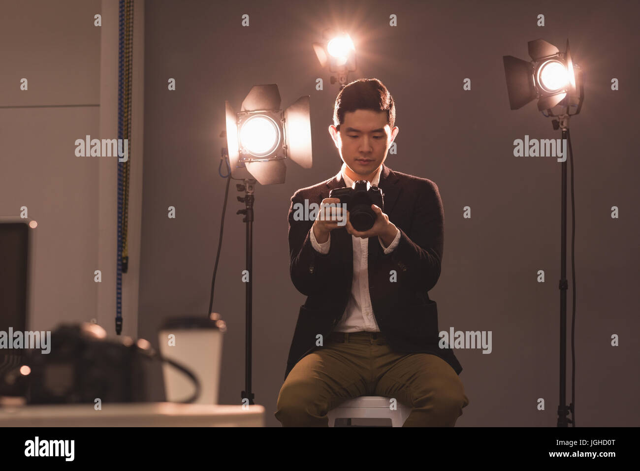 Male photographer holding camera while sitting on stool at illuminated ...