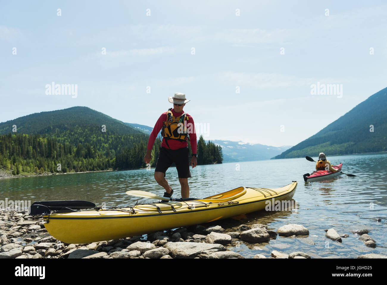 Man walking towards kayak with woman kayaking in background against sky ...