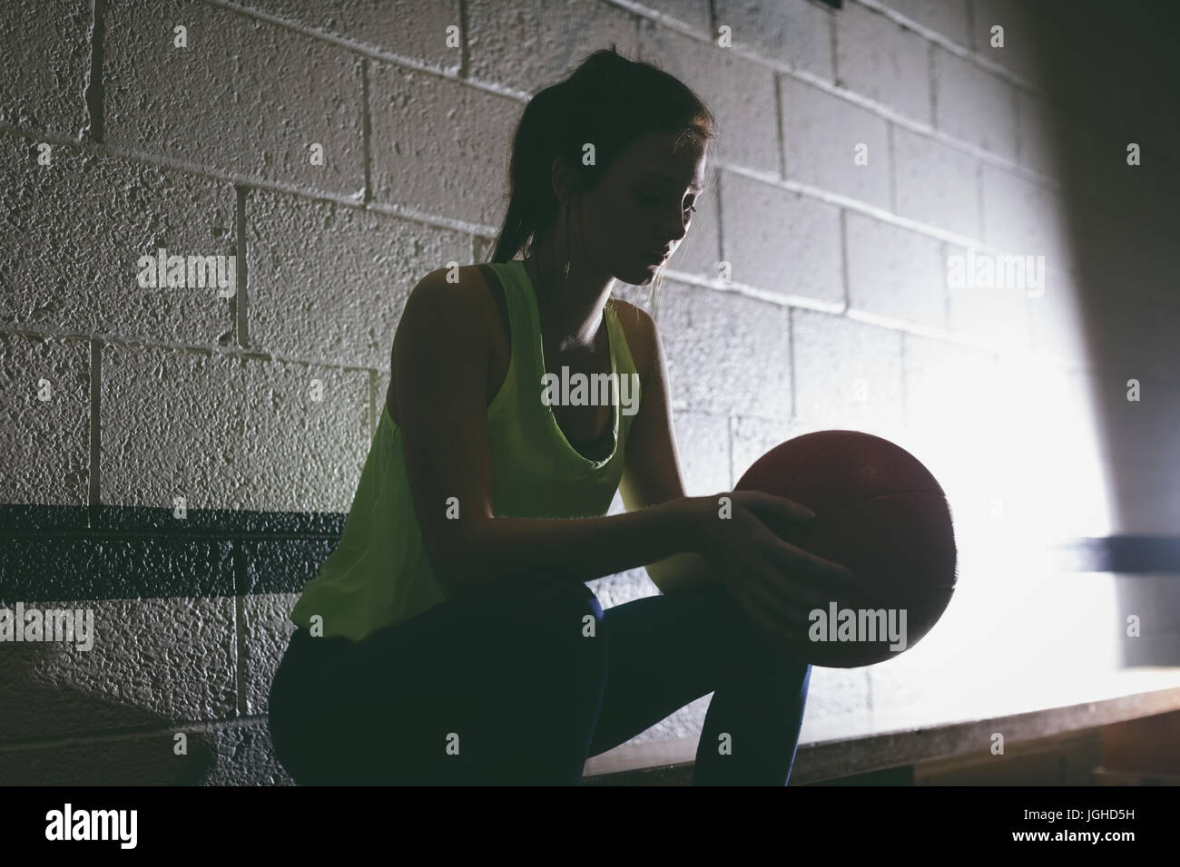 Female player holding basketball by wall while sitting on bench Stock ...