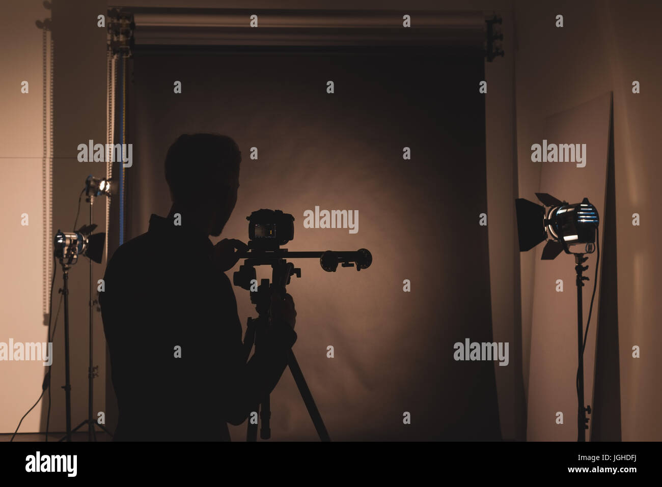 Rear view of man adjusting camera while standing against backdrop at ...
