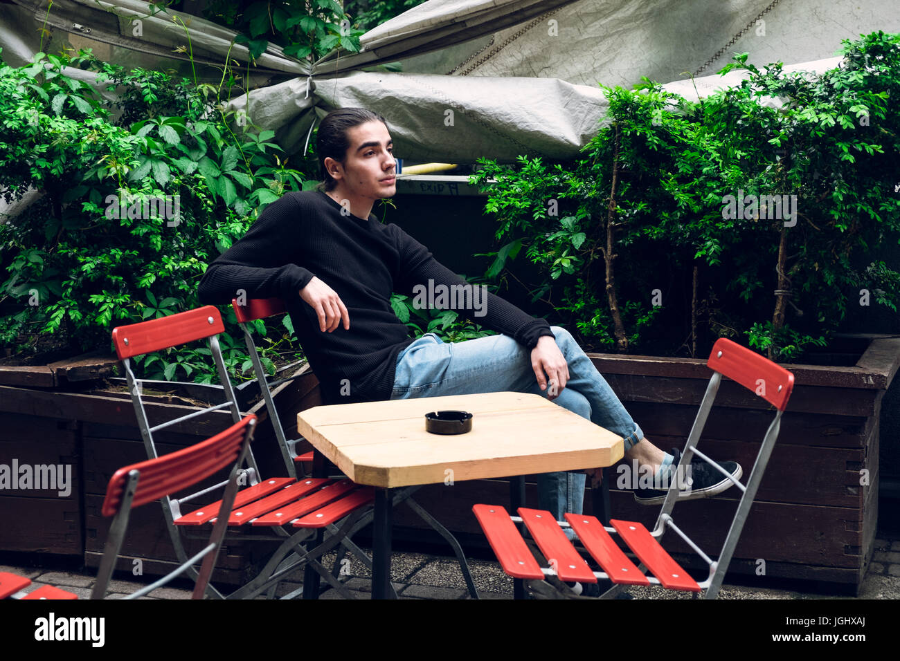 Young man sitting in a red chair in outdoor Stock Photo - Alamy