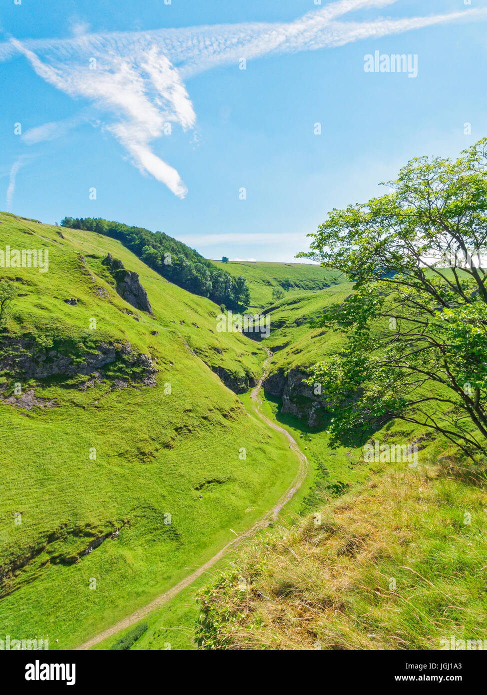 A footpath at the bottom of a lush, green, valley winds around rock ...
