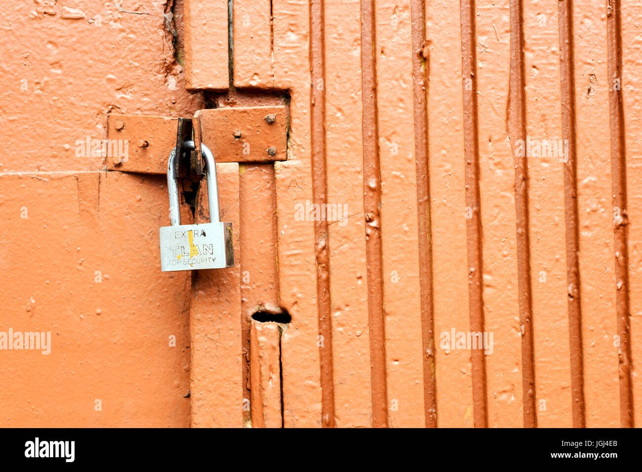 Single padlock locking an orange painted rustic door made from wood and ...