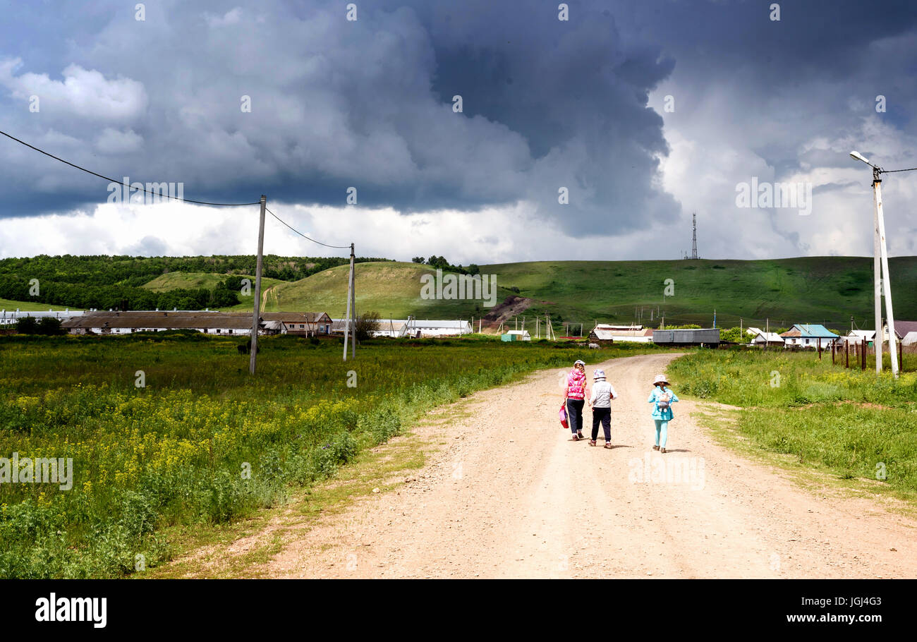 Three young girls walk along a dusty road towards ominous rain cloud ...