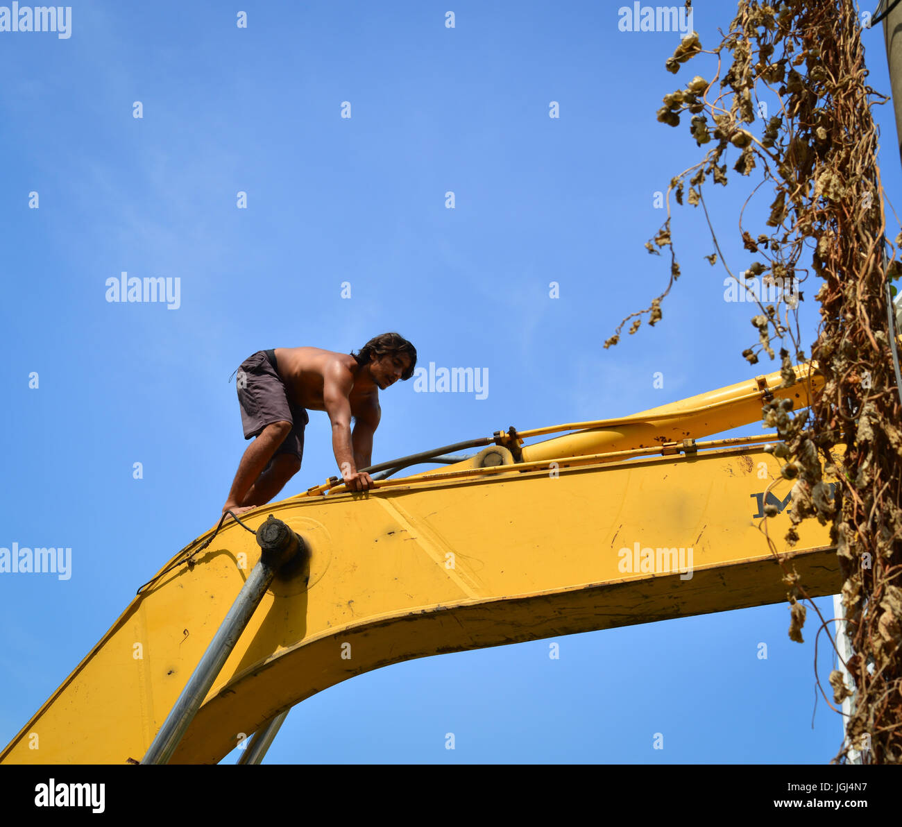 An Indian young man climbing on the construction machine at sunny day ...