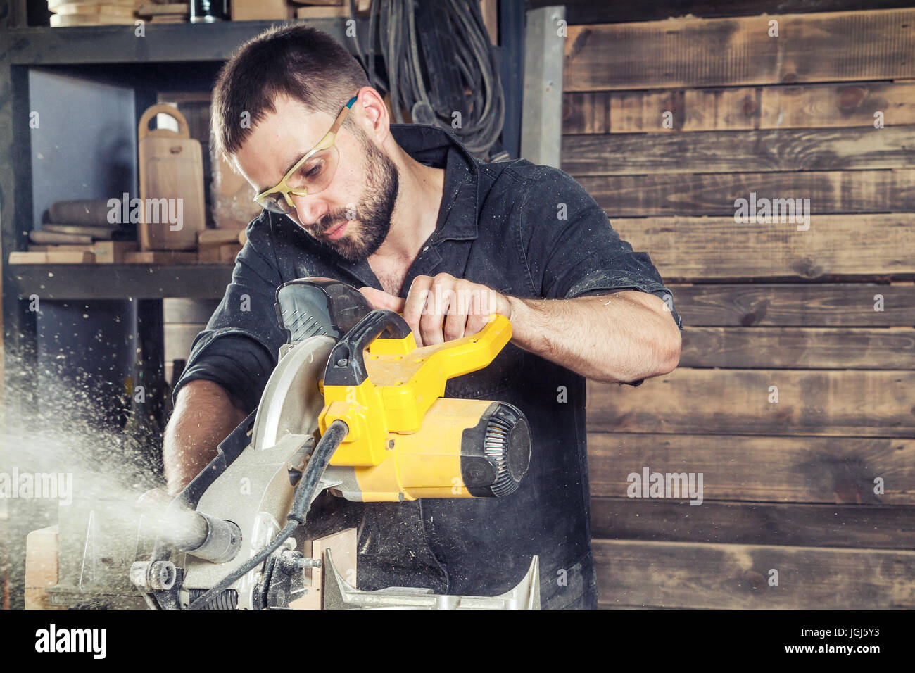 A young male construction carpenter saws a modern circular saw with a ...
