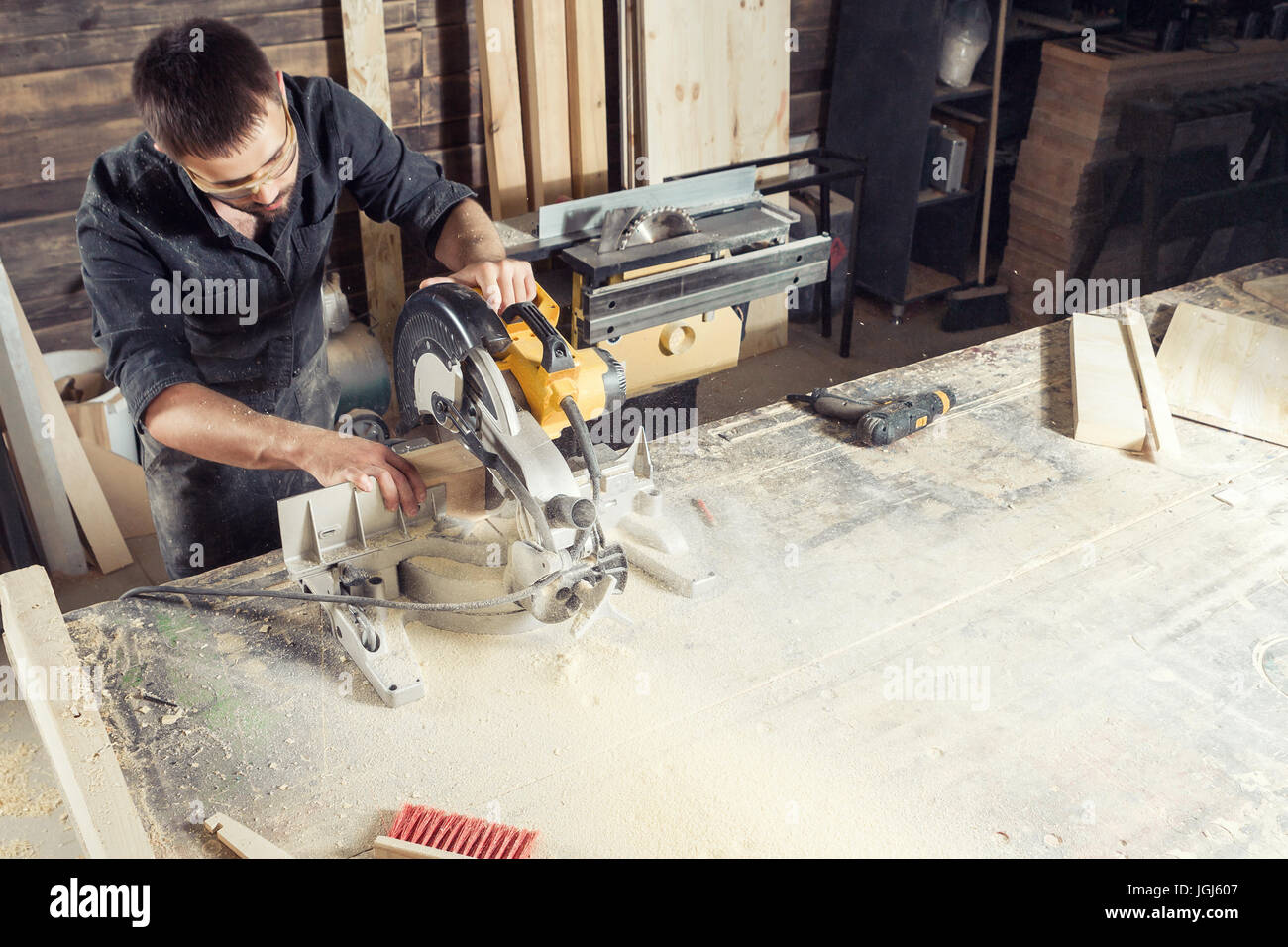 A young male carpenter builder saws a modern circular saw a wooden ...