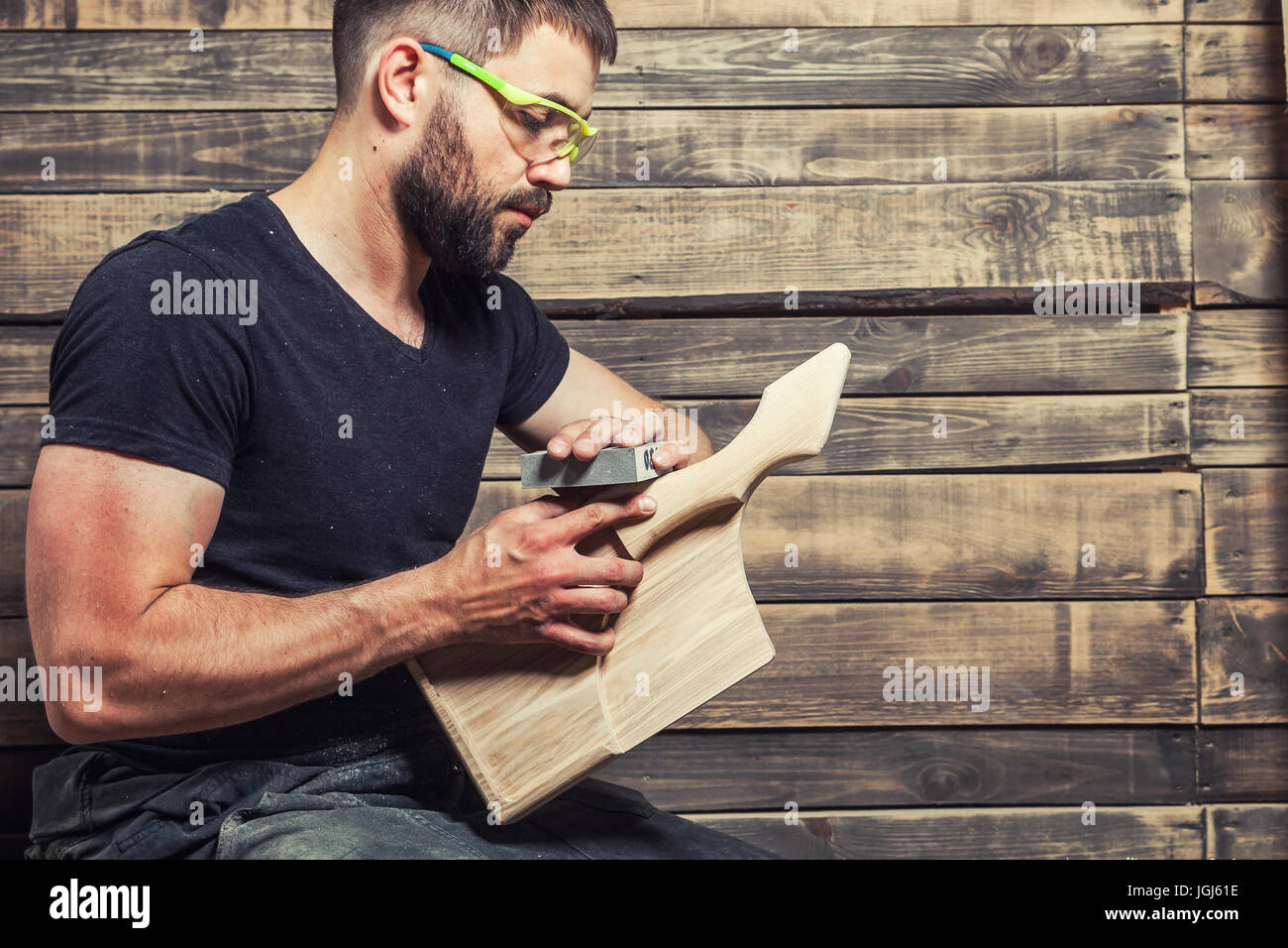 Young man carpenter with a beard sitting on a bench lining a wooden ...