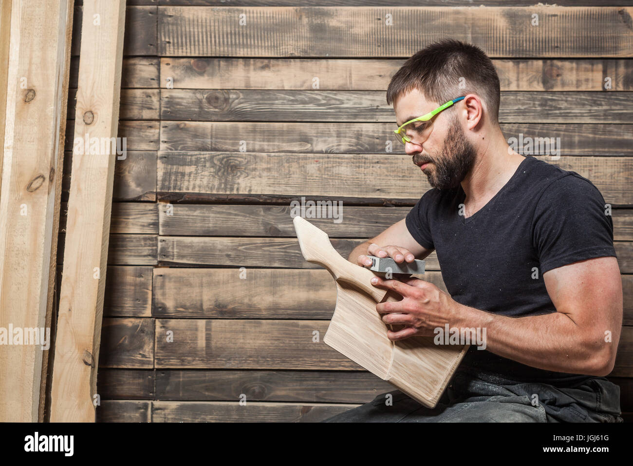 Young man carpenter with a beard sitting on a bench lining a wooden ...