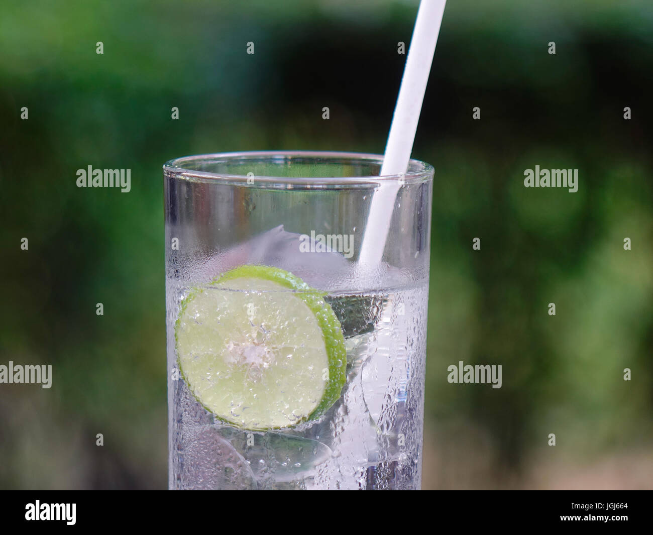 Glass of lime juice with white straw at the summer garden. Close up ...