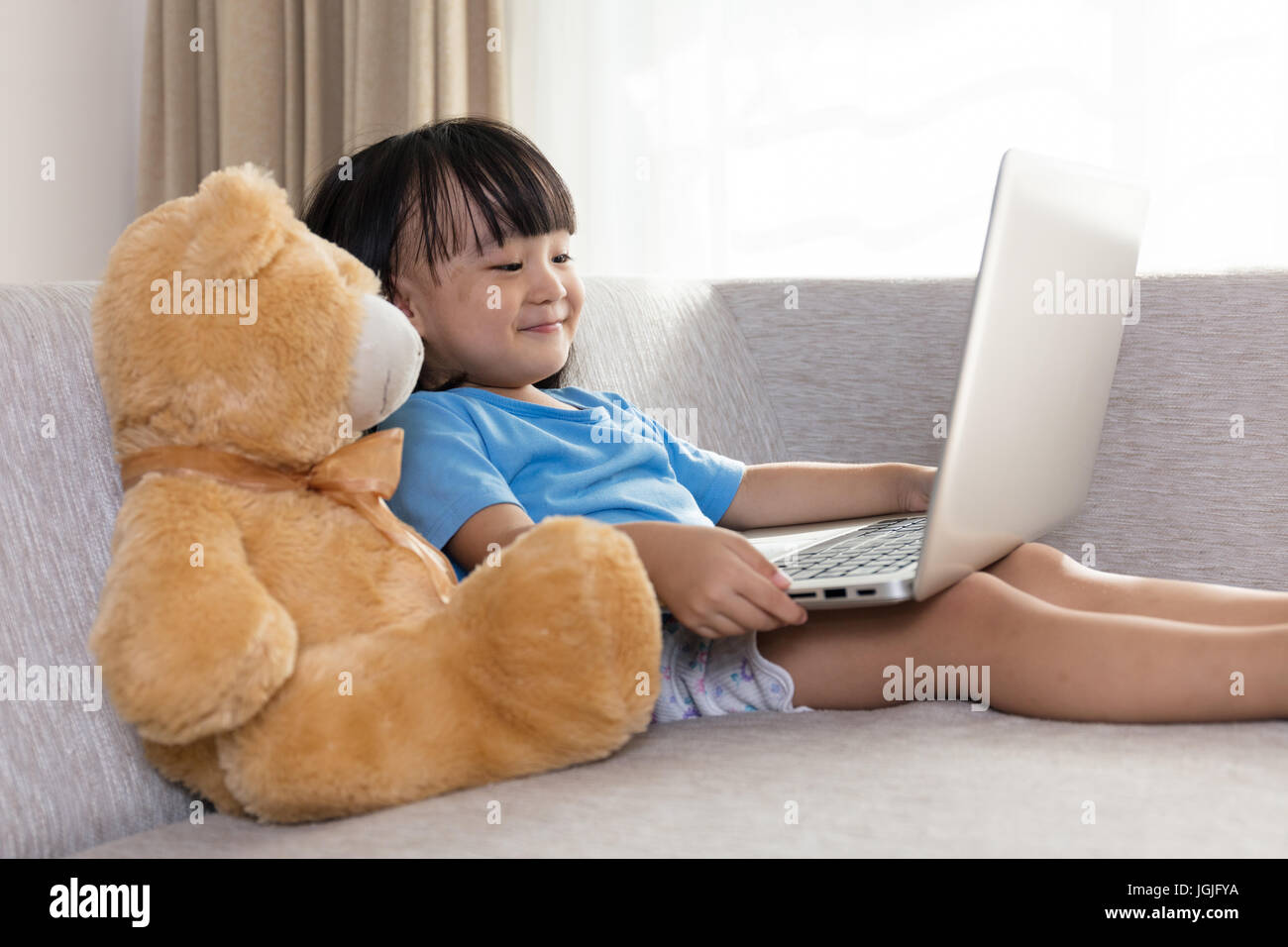 Asian Chinese little girl using laptop with teddy bear in the living ...