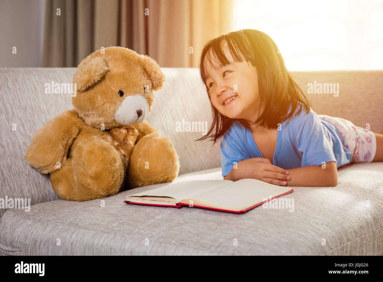 Smiling Asian Chinese little girl reading book with teddy bear on the ...