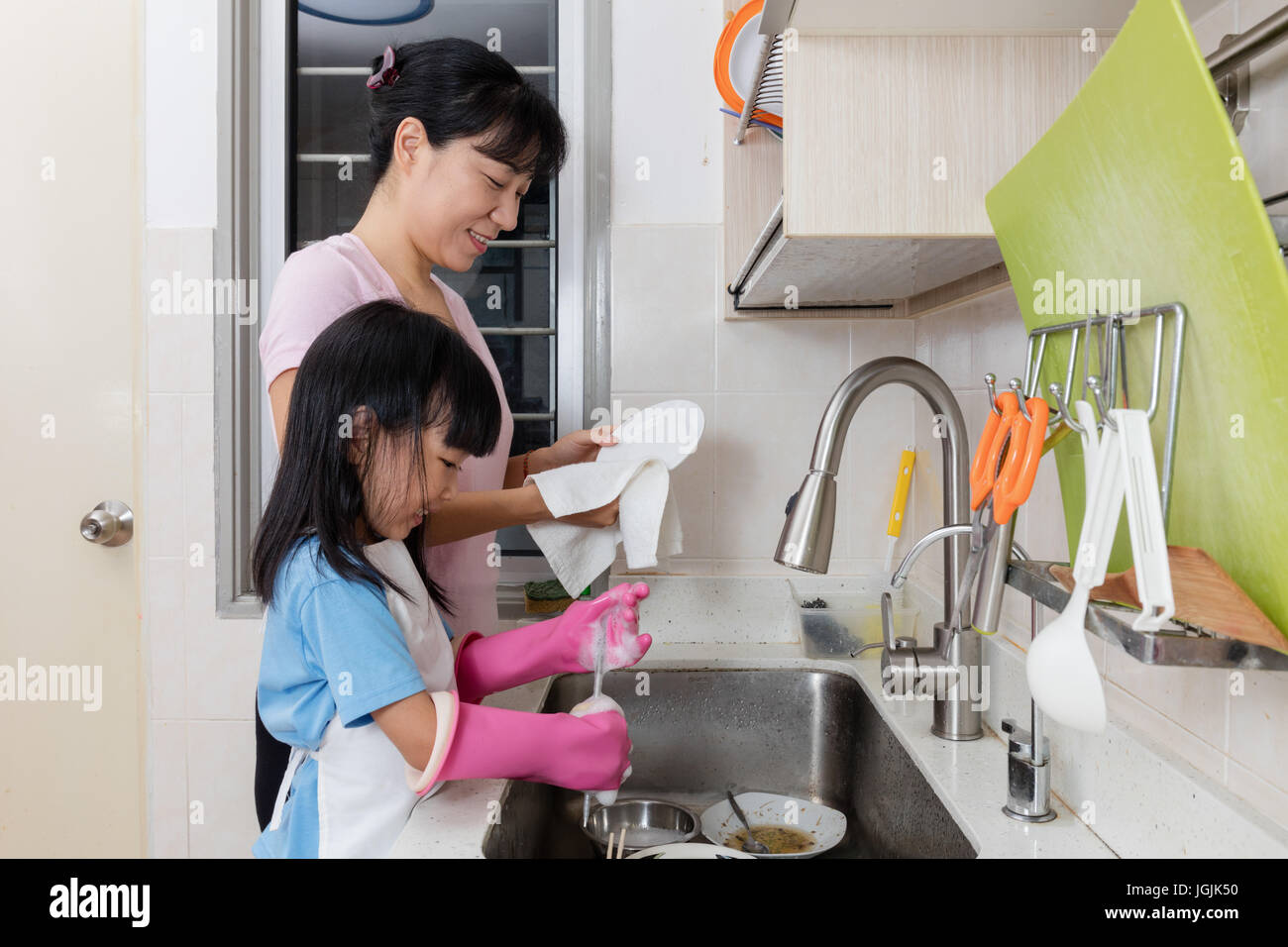 Asian Chinese little girl helping mother washing dishes in the kitchen ...