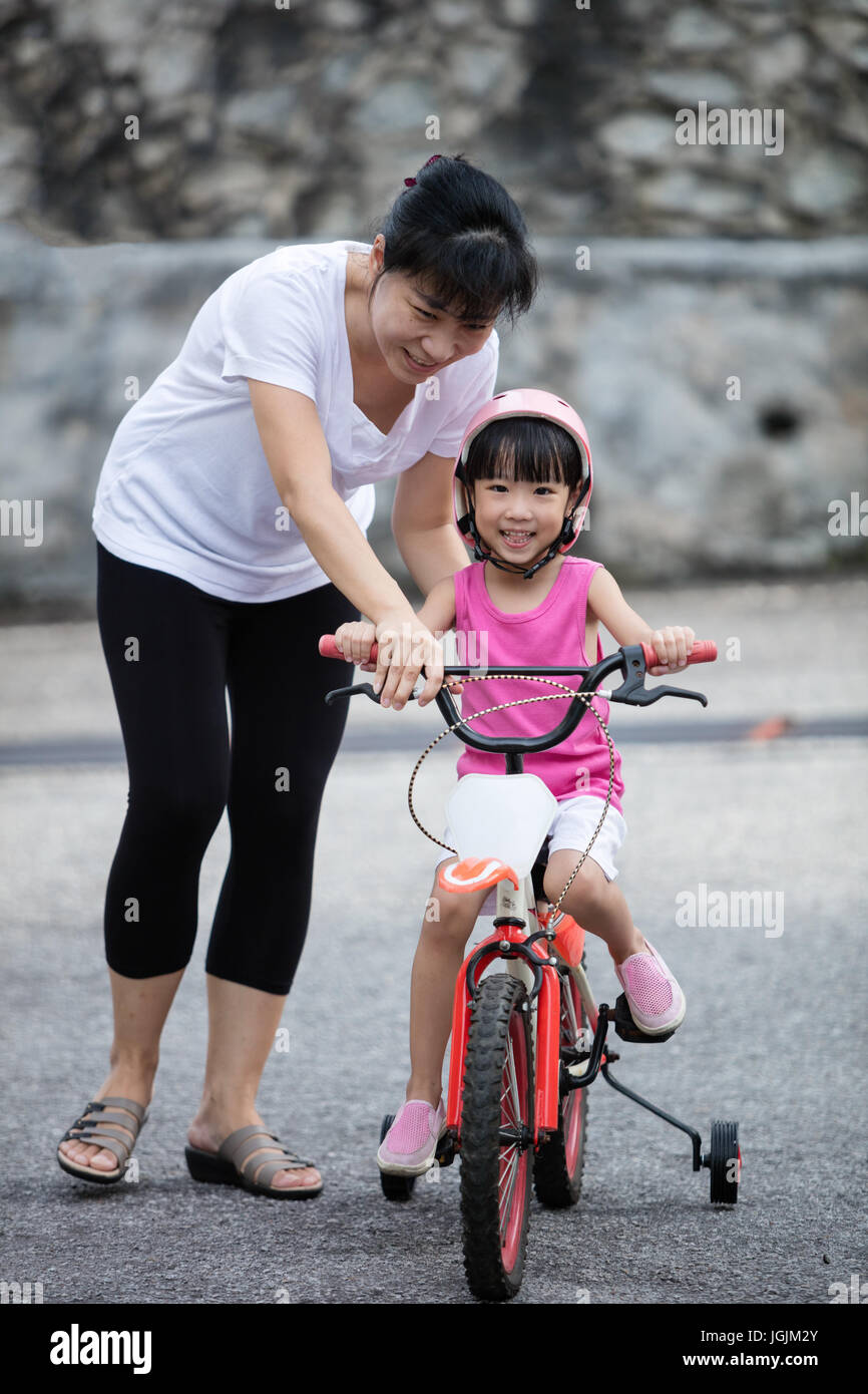 Asian Chinese little girl riding bicycle with mom guide on tar road ...