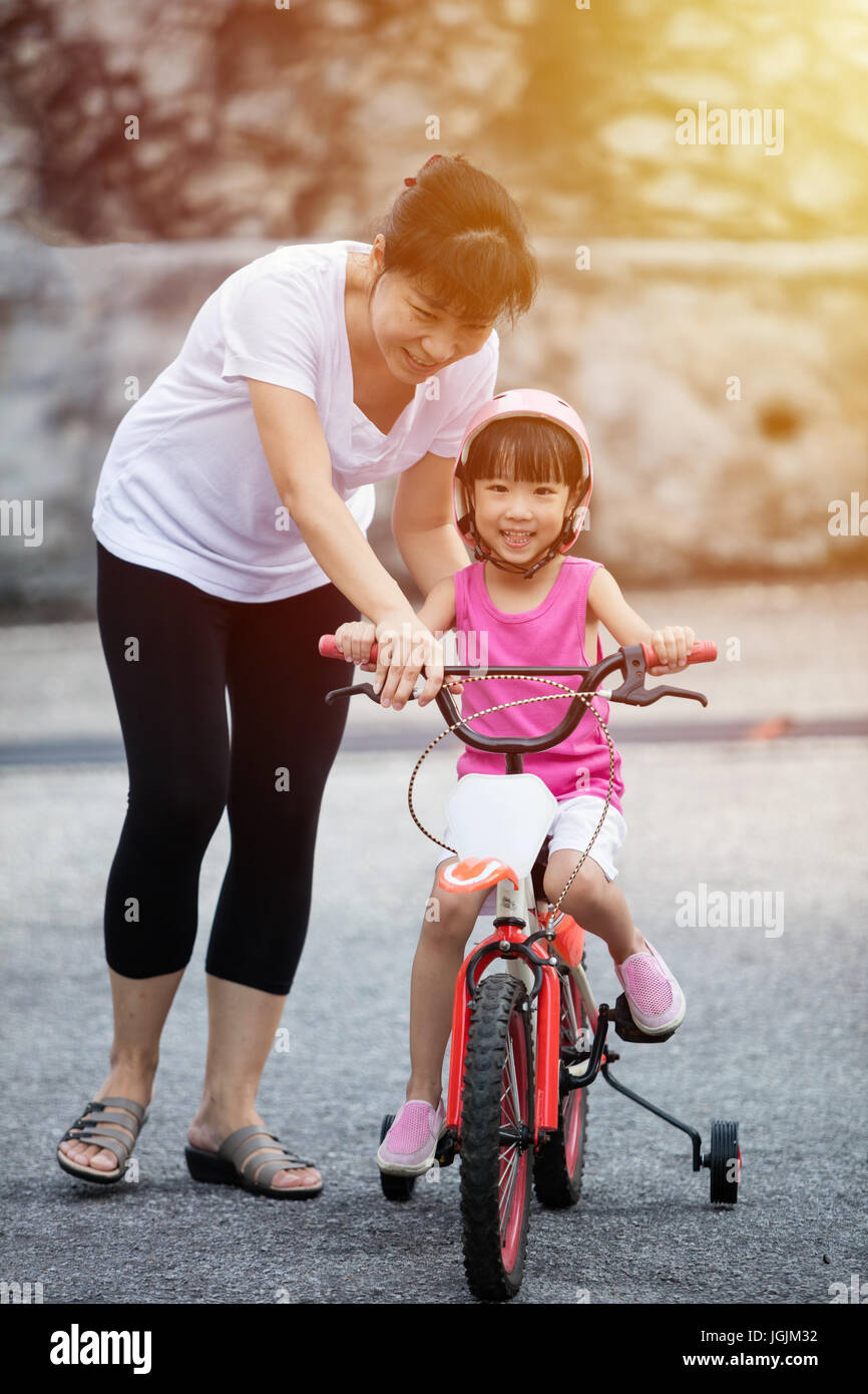 Asian Chinese little girl riding bicycle with mom guide on tar road ...