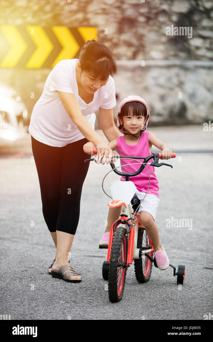 Asian Chinese little girl riding bicycle with mom guide on tar road ...