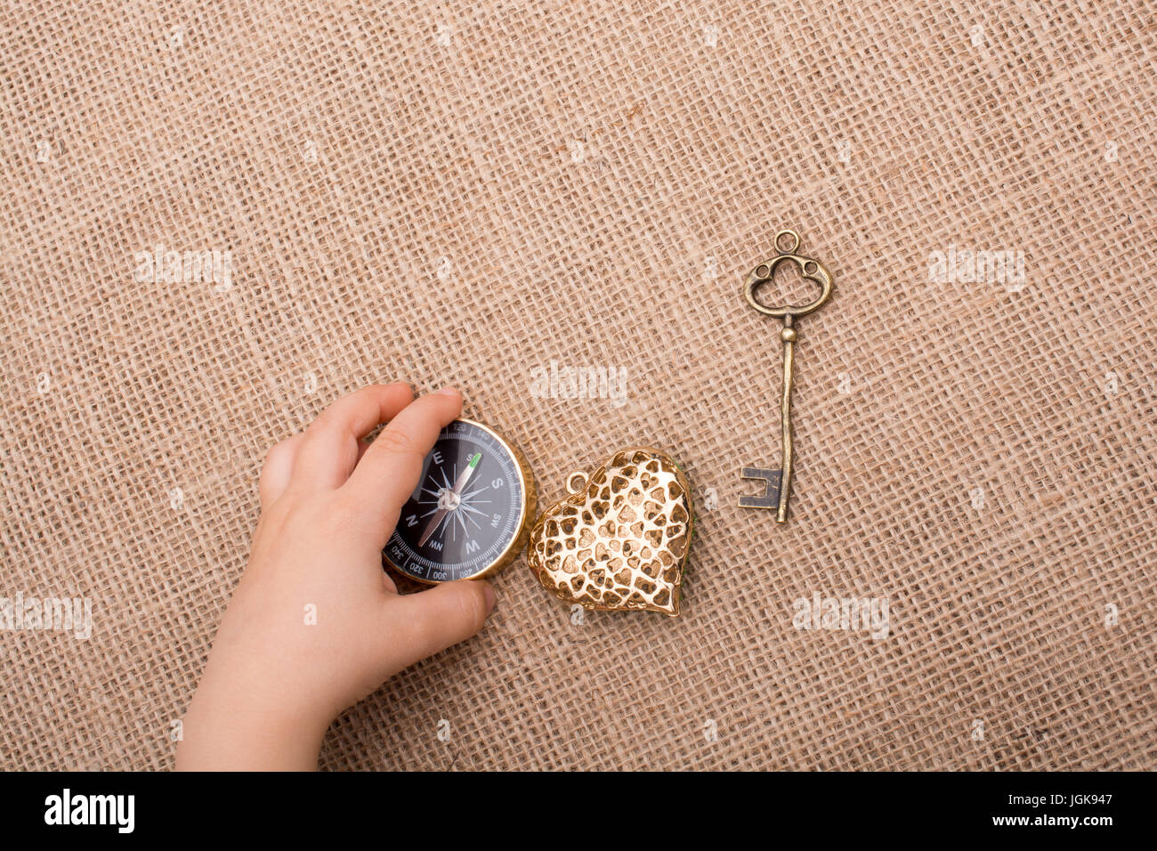 Compass, key and a heart shaped object beside a hand Stock Photo - Alamy