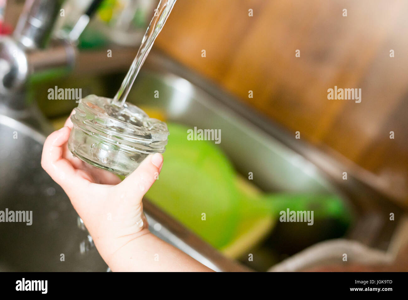 hand of a baby pouring water into a small jar or another little ...