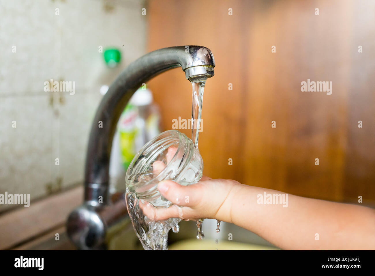 hand of a baby pouring water into a small jar or another little ...