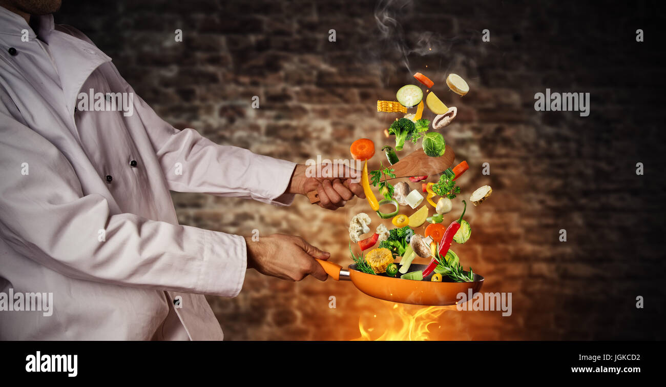Closeup of chef cooker preparing vegetable on fire, flying motion ...