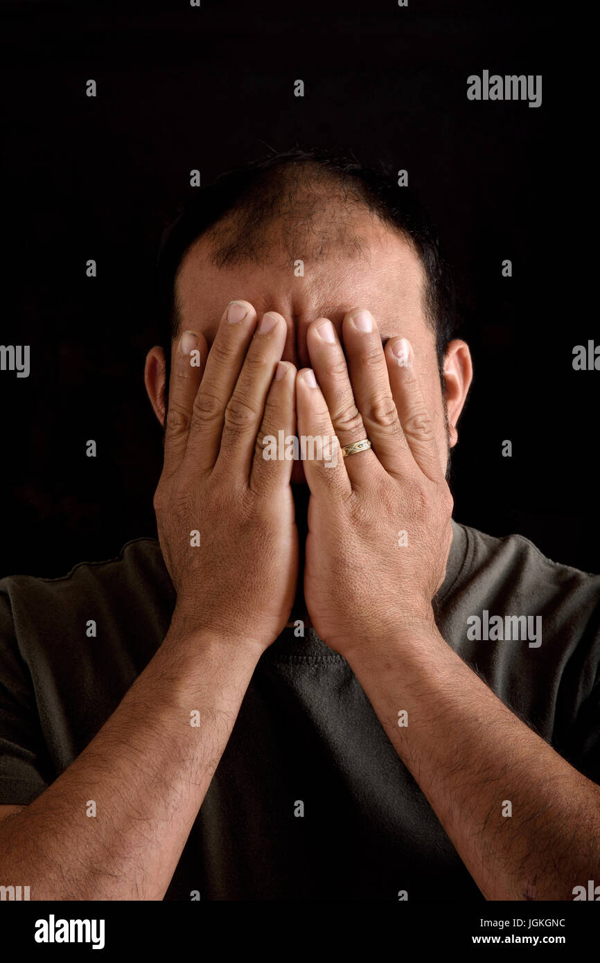 Man covering his face on black background Stock Photo - Alamy