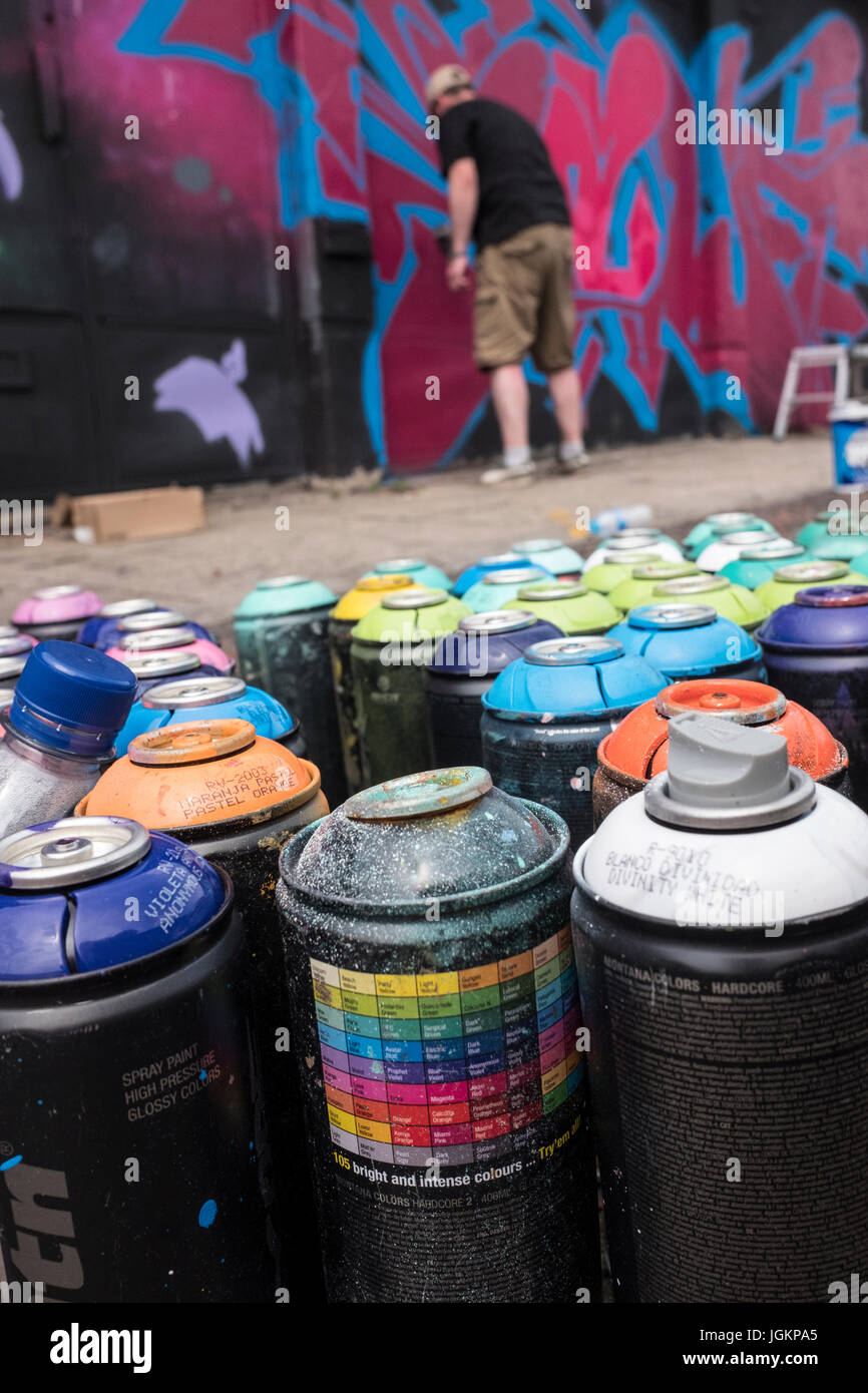 Graffiti artist painting a mural on a wall with spray cans in the ...