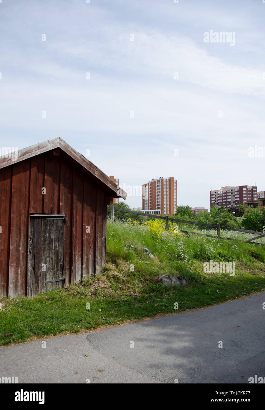 an old-fashioned red painted shed beside a sidewalk with the city ...