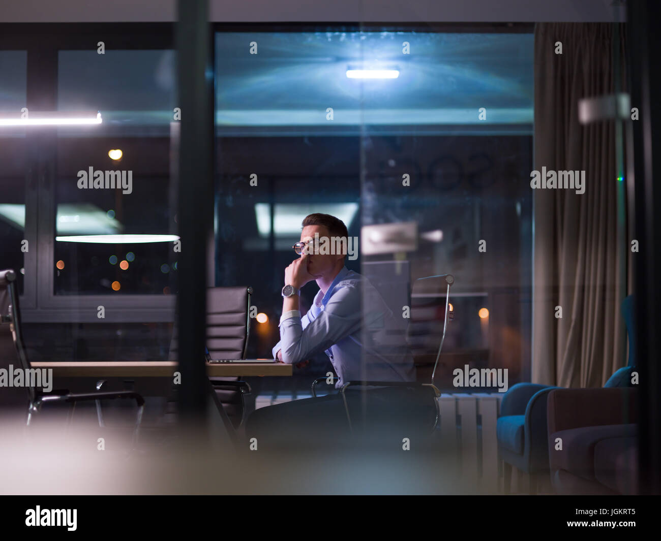 Young man working on laptop at night in dark office. The designer works ...