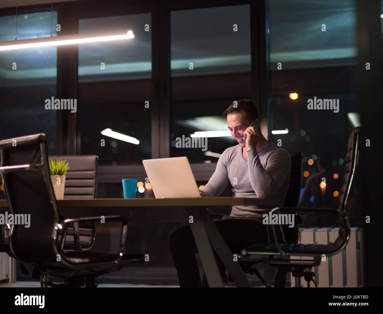 Young man working on laptop at night in dark office. The designer works ...