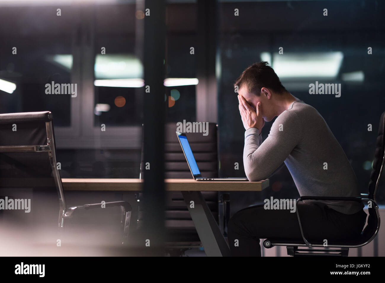 Young man working on laptop at night in dark office. The designer works ...