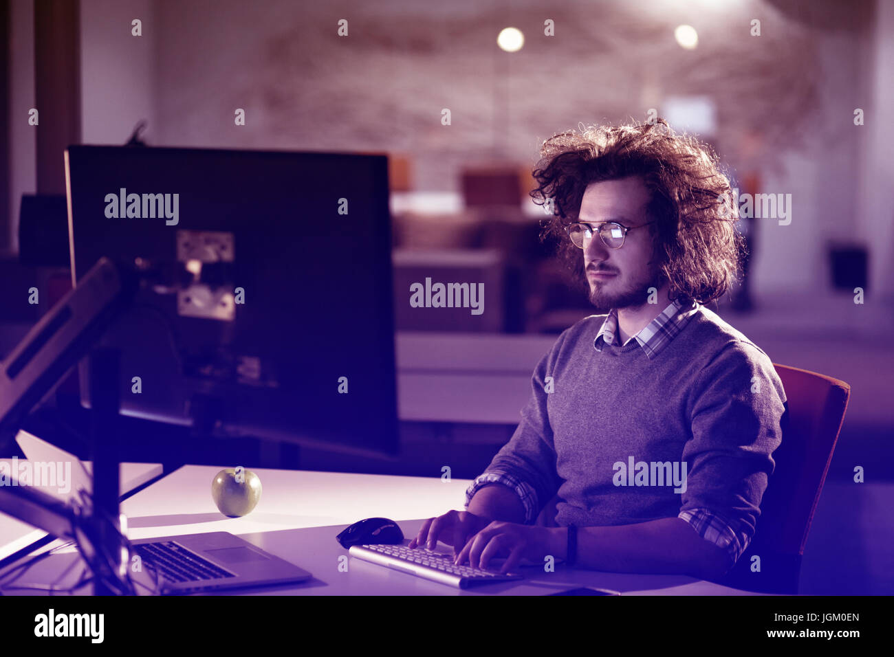 Young man working on computer at night in dark office. The designer ...