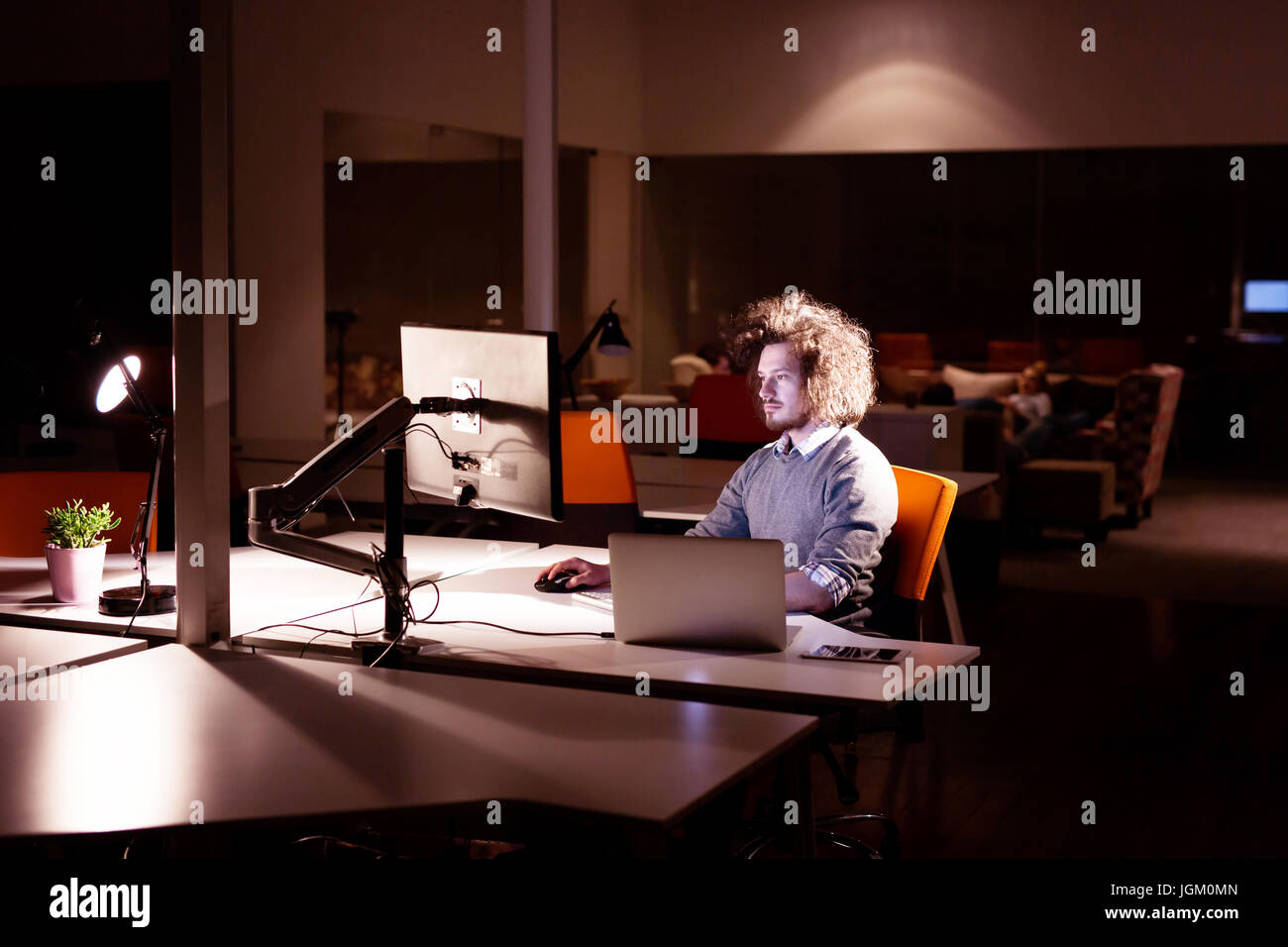 Young man working on computer at night in dark office. The designer ...