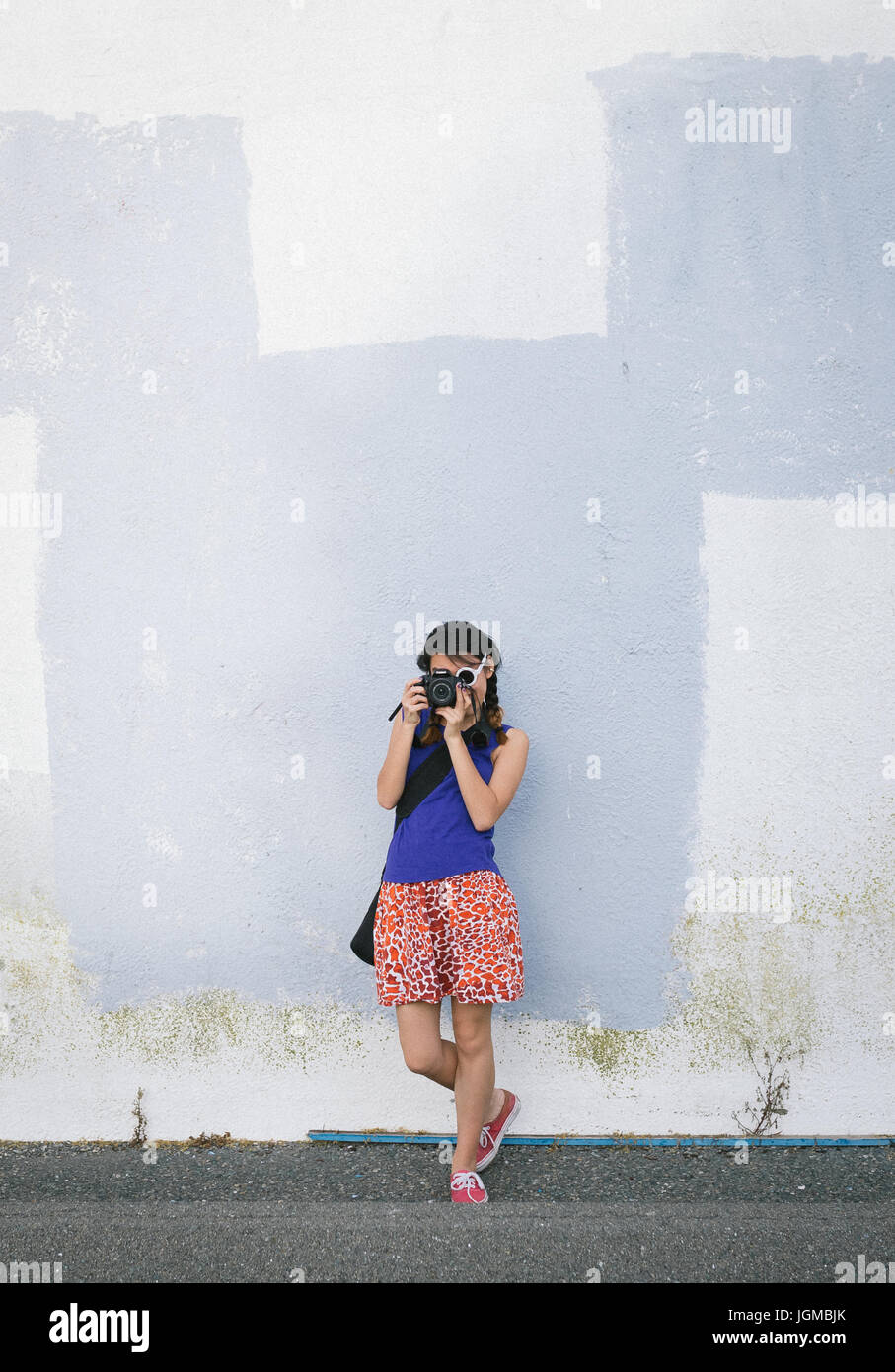 Girl holding up camera to her face while standing in front of a blank ...