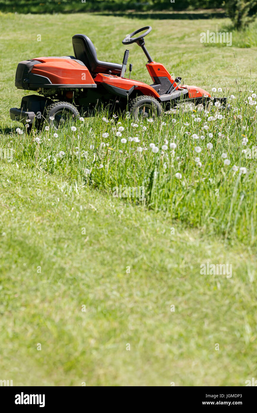 red lawn mower at rest on a farm meadow against green grass background ...