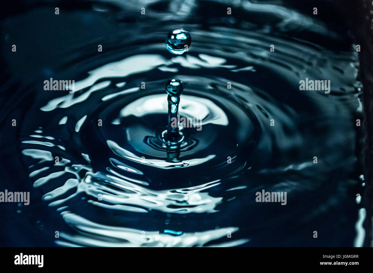Water drop splashing into smooth water causing ripples in a calm ...