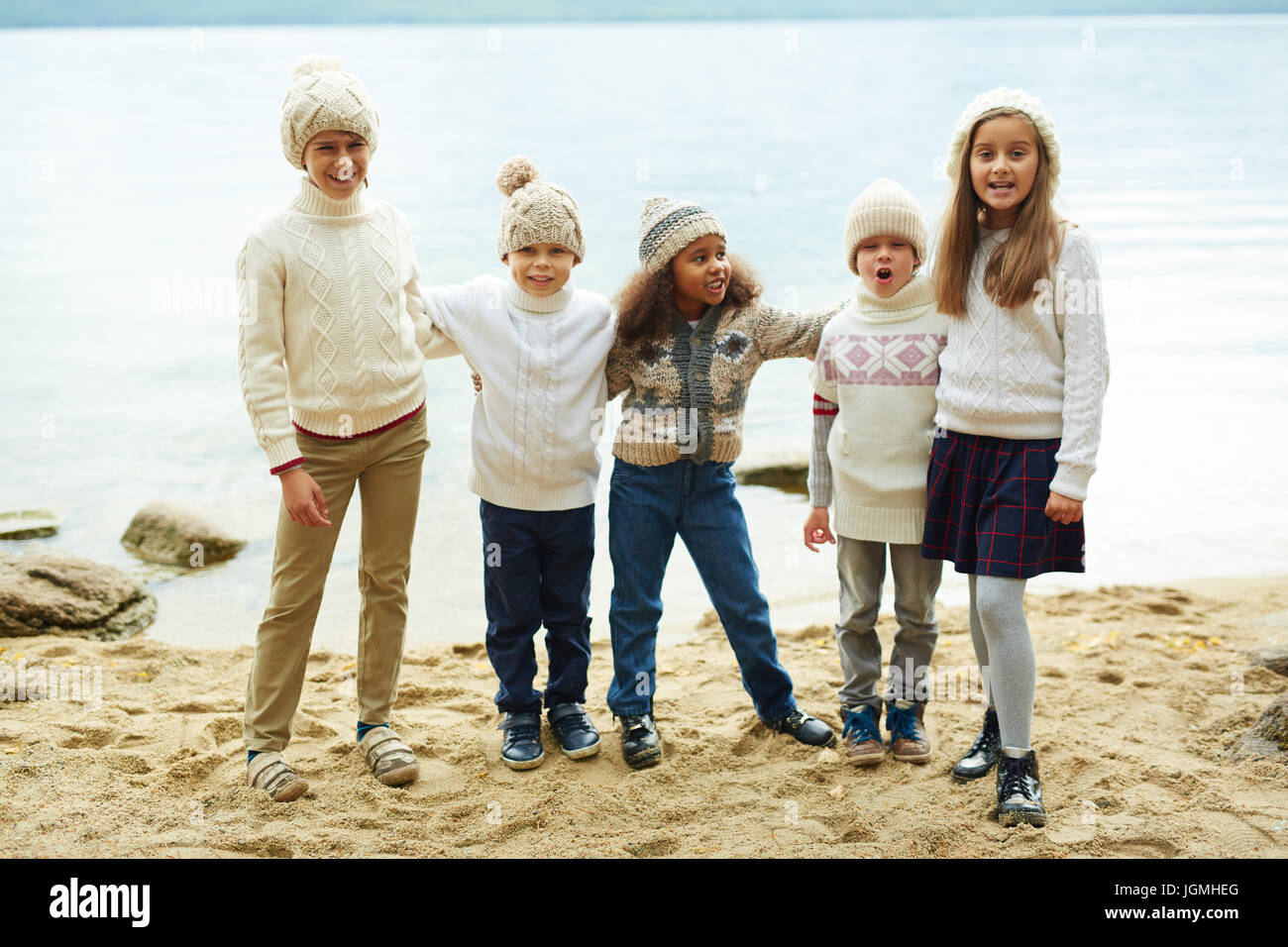 Group of cheerful children standing by lake in row posing playfully to ...