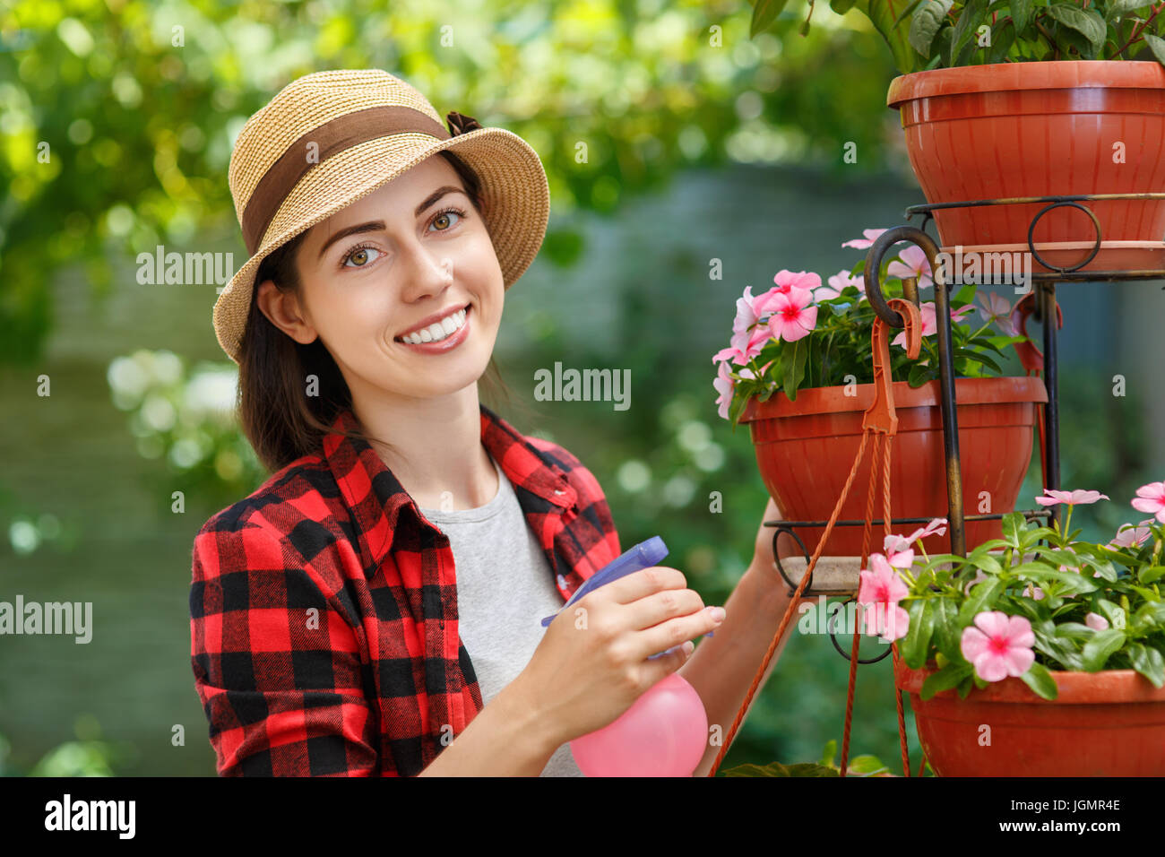 portrait of happy young woman gardener spraying water on plants. Girl ...
