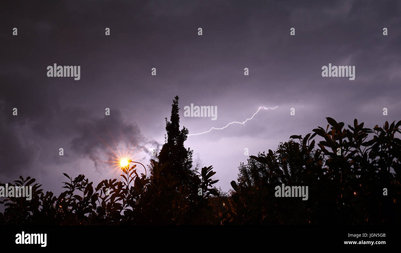 Lightning storm at night with tree line and street light in the ...