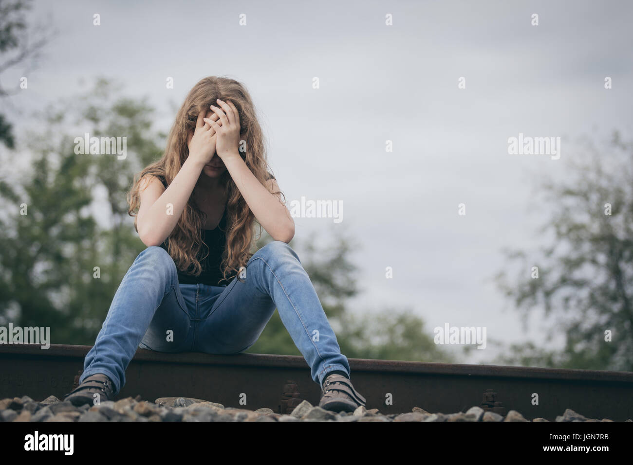 Portrait of young sad ten girl sitting outdoors on the railway at the ...