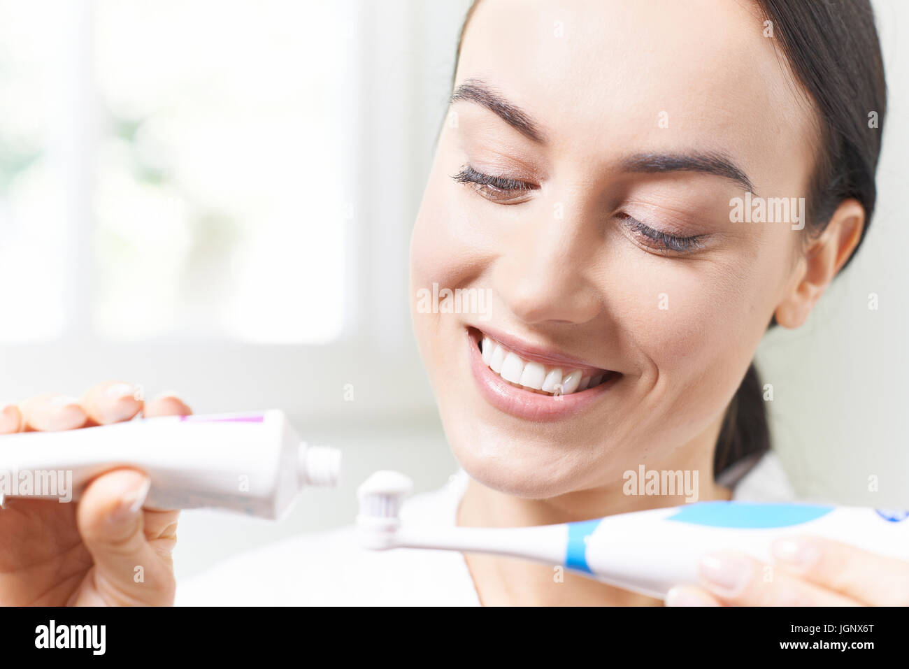 Woman Squeezing Toothpaste Onto Electric Toothbrush In Bathroom Stock ...