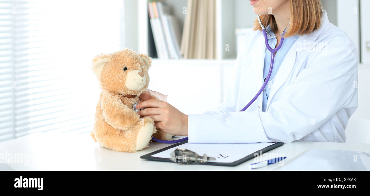 Female doctor examining a Teddy bear patient by stethoscope. Children ...