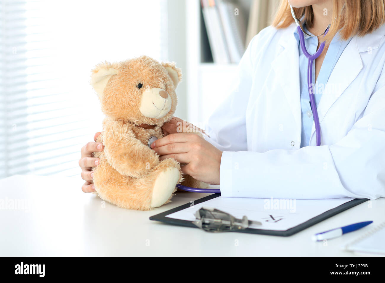 Female doctor examining a Teddy bear patient by stethoscope. Children ...