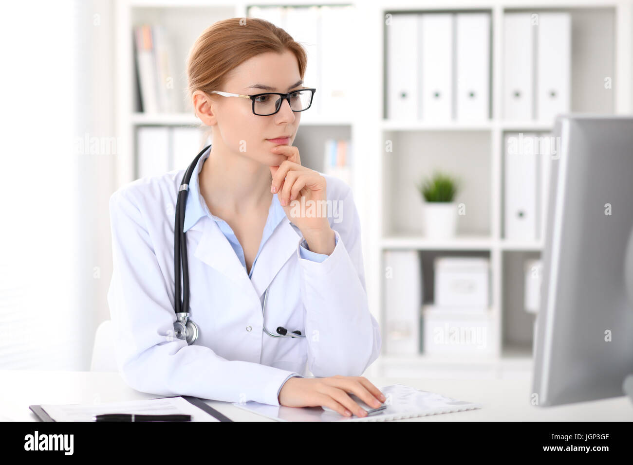 Young brunette female doctor sitting at the table and working by ...